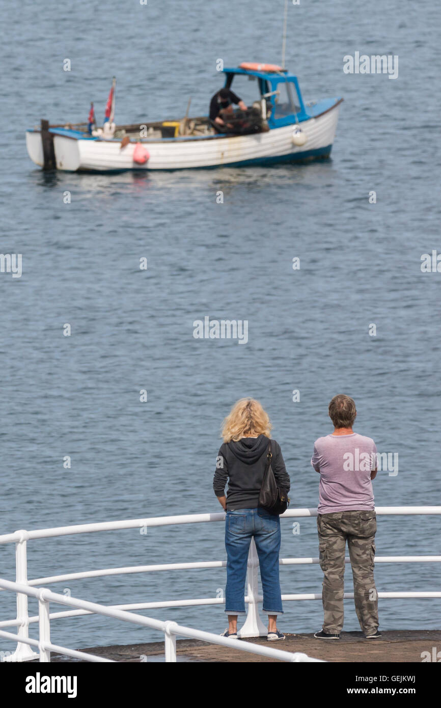 man and woman looking out to sea at a small fishing boat Stock Photo ...