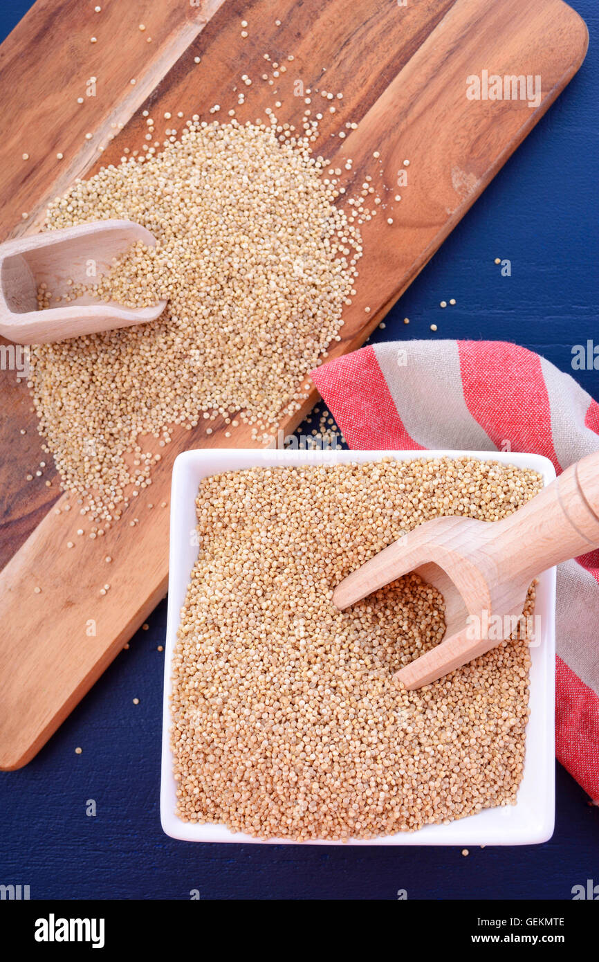 White grain quinoa with wooden scoops and chopping board on dark blue ...