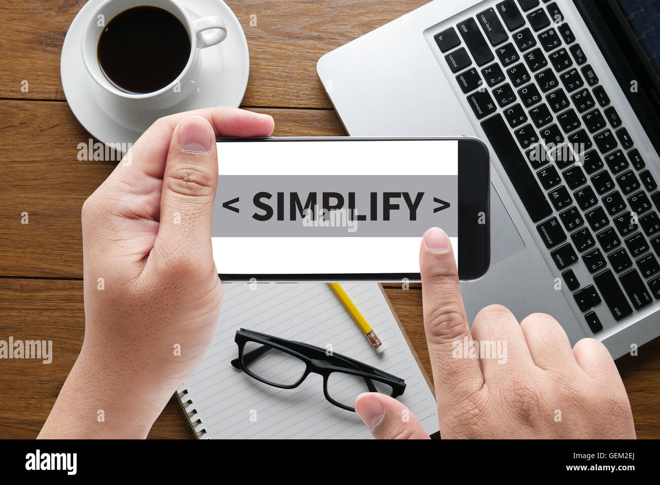 SIMPLIFY message on hand holding to touch a phone, top view, table ...