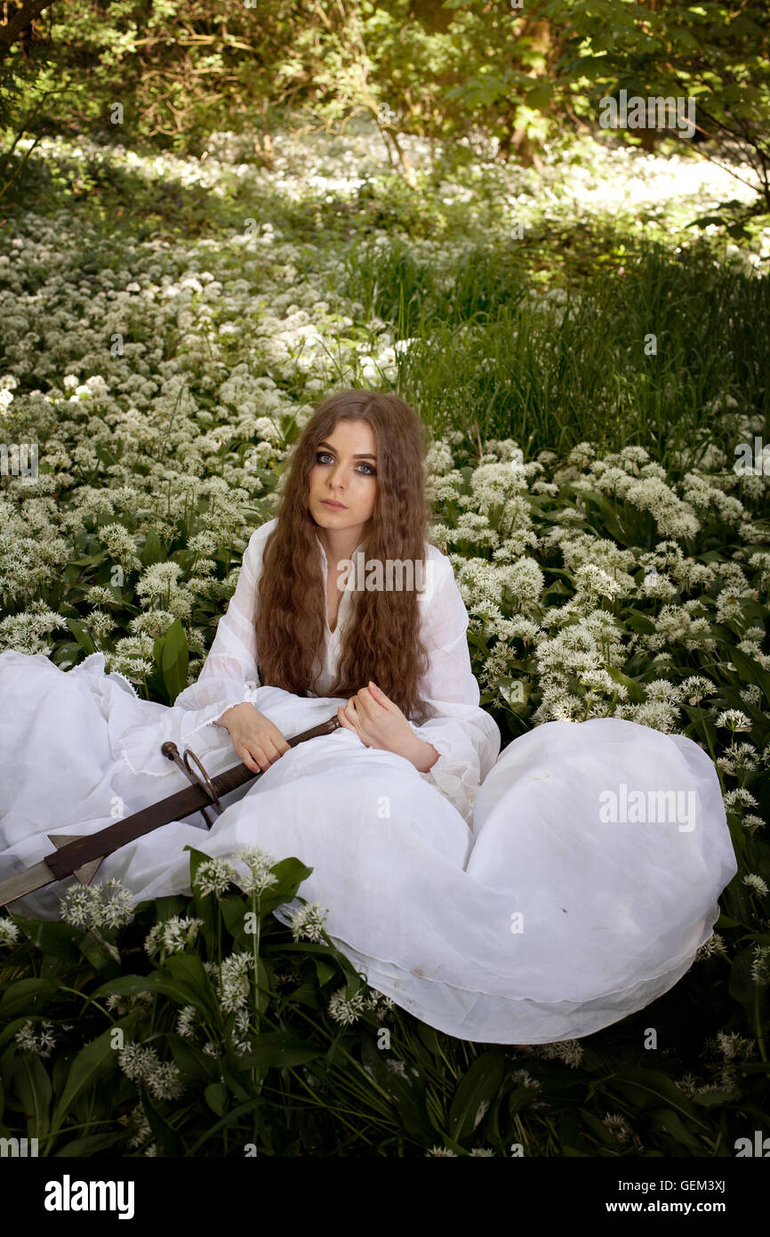 Beautiful young woman in a forest holding a long sword wearing long ...