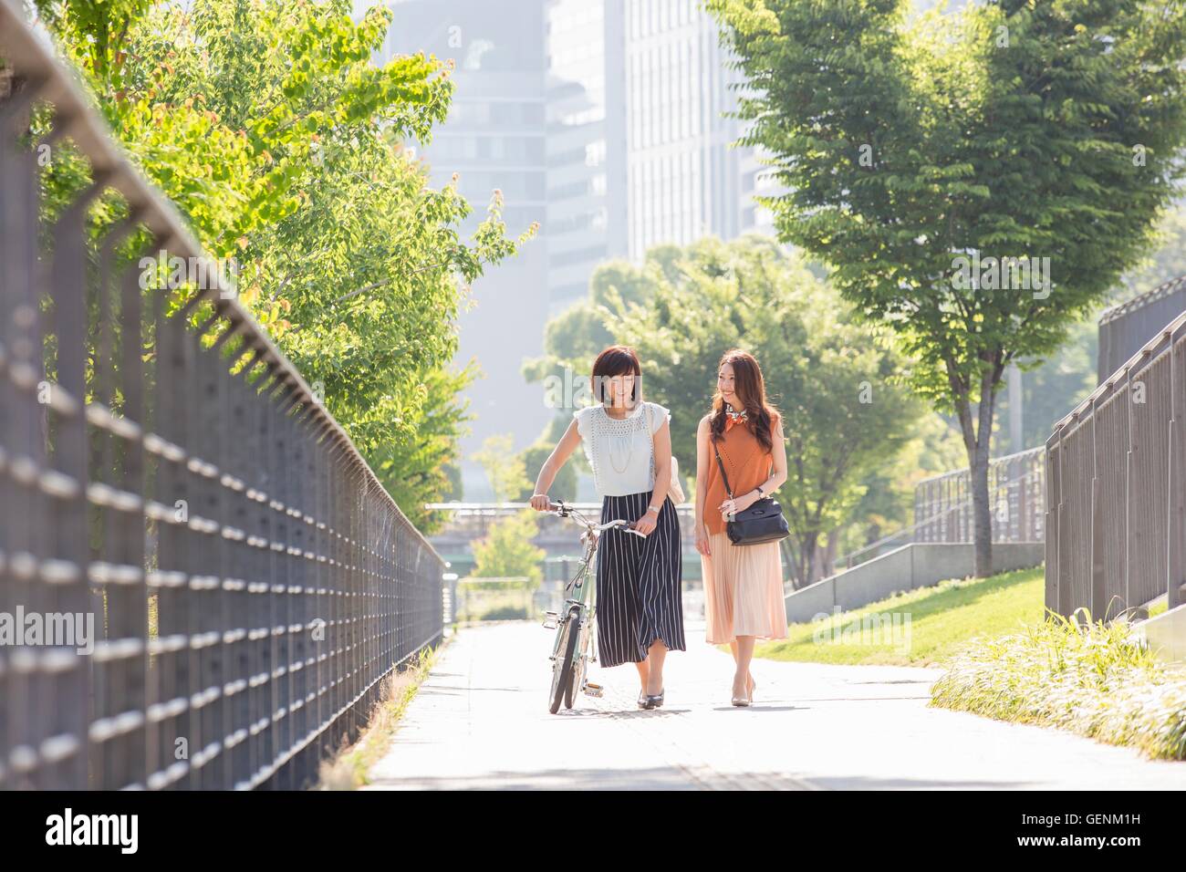 A woman walking her bicycle and the other woman walking Stock Photo - Alamy