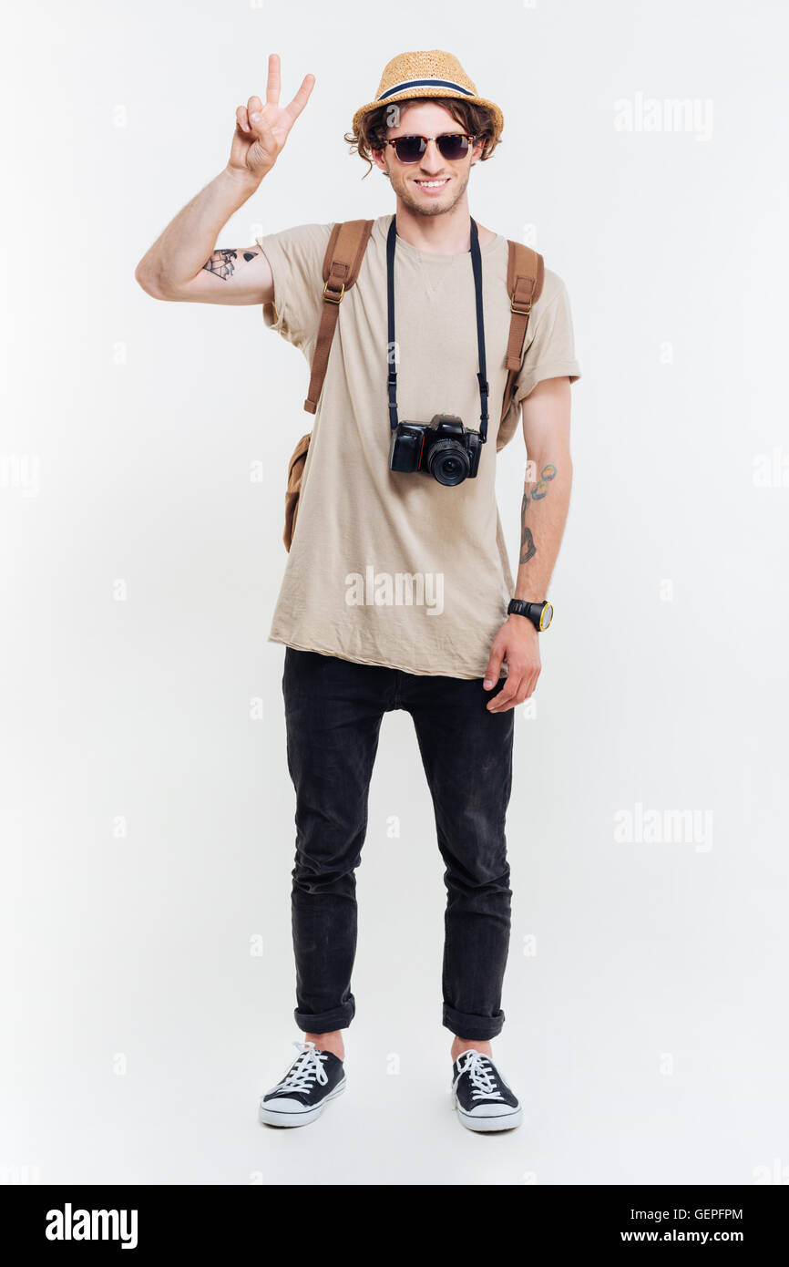 Full length of smiling young man standing and showing peace sign over ...