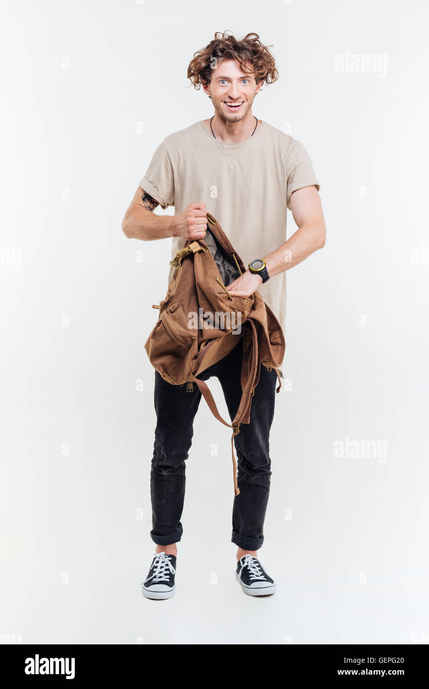 Young smiling man standing and getting something out of his backpack ...