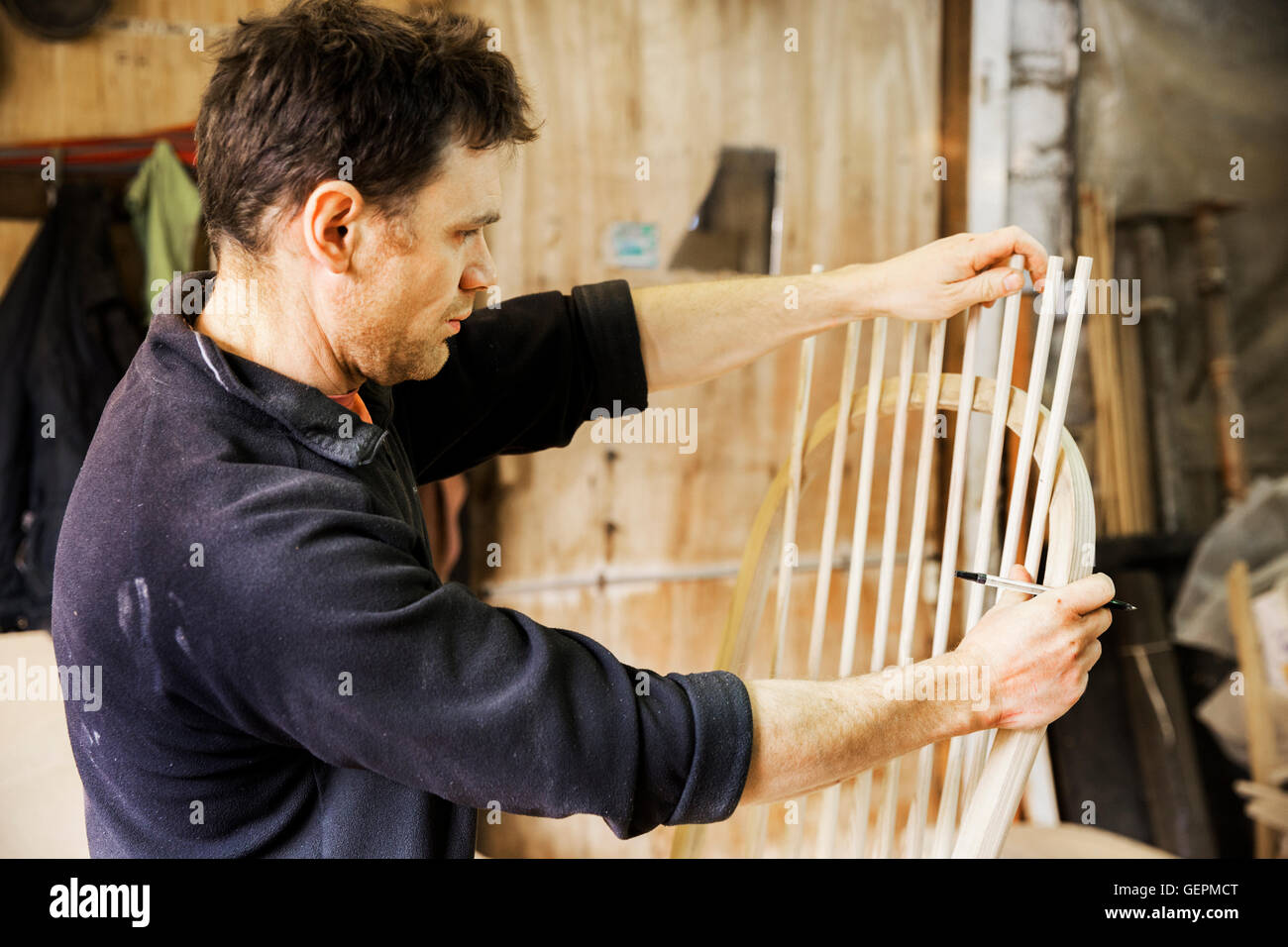Man standing in a carpentry workshop, working on a wooden chair back ...