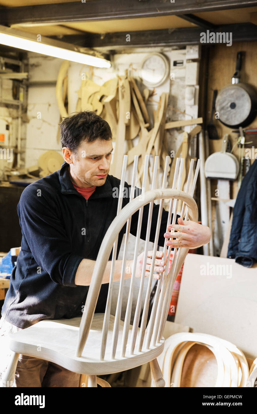 Man standing in a carpentry workshop, working on a wooden chair back ...
