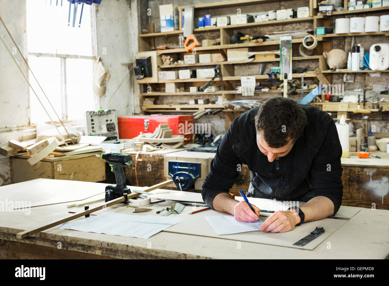 Man standing at a work bench in a carpentry workshop, writing a ...