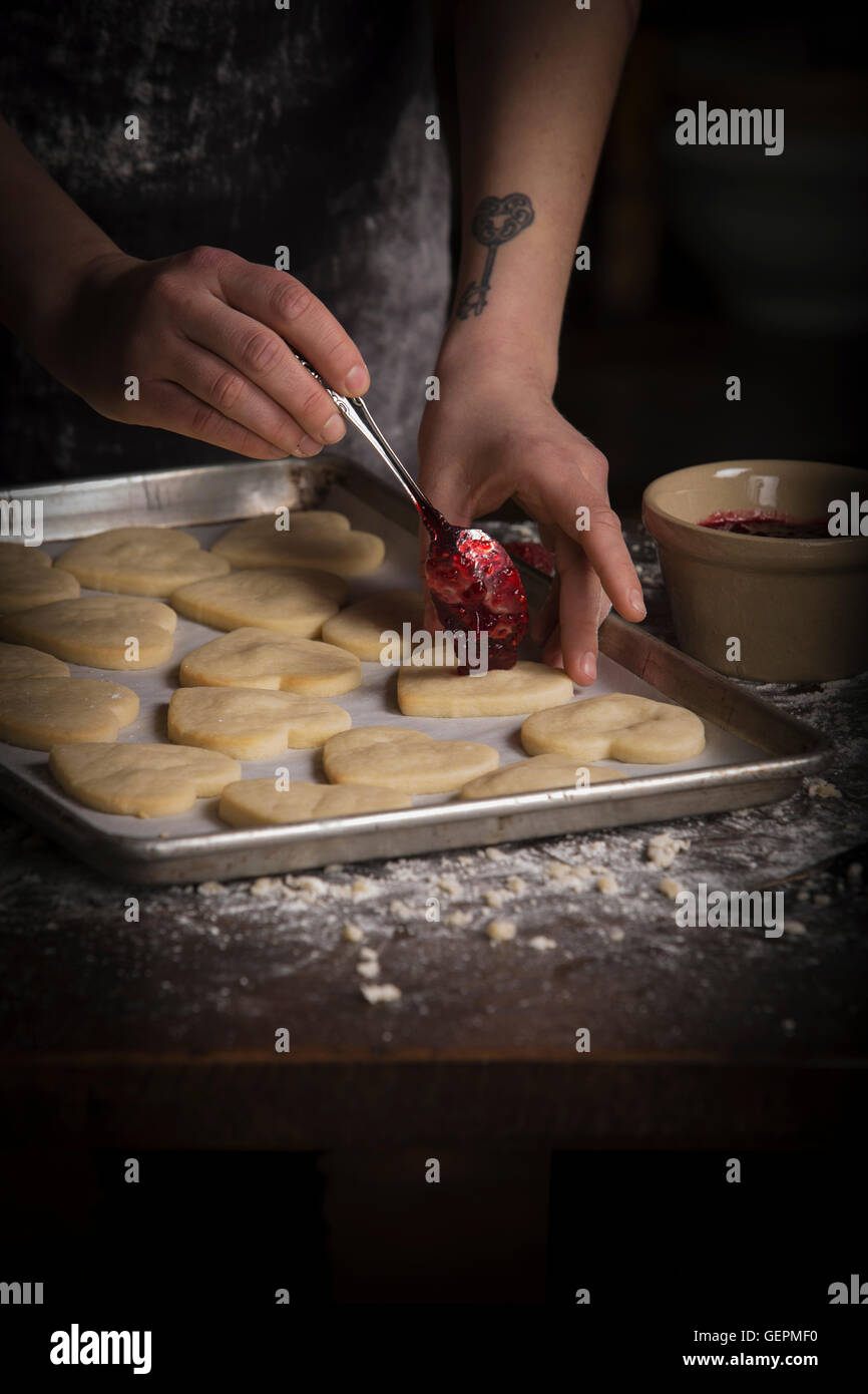 Valentine's Day baking, woman spreading raspberry jam on heart shaped ...