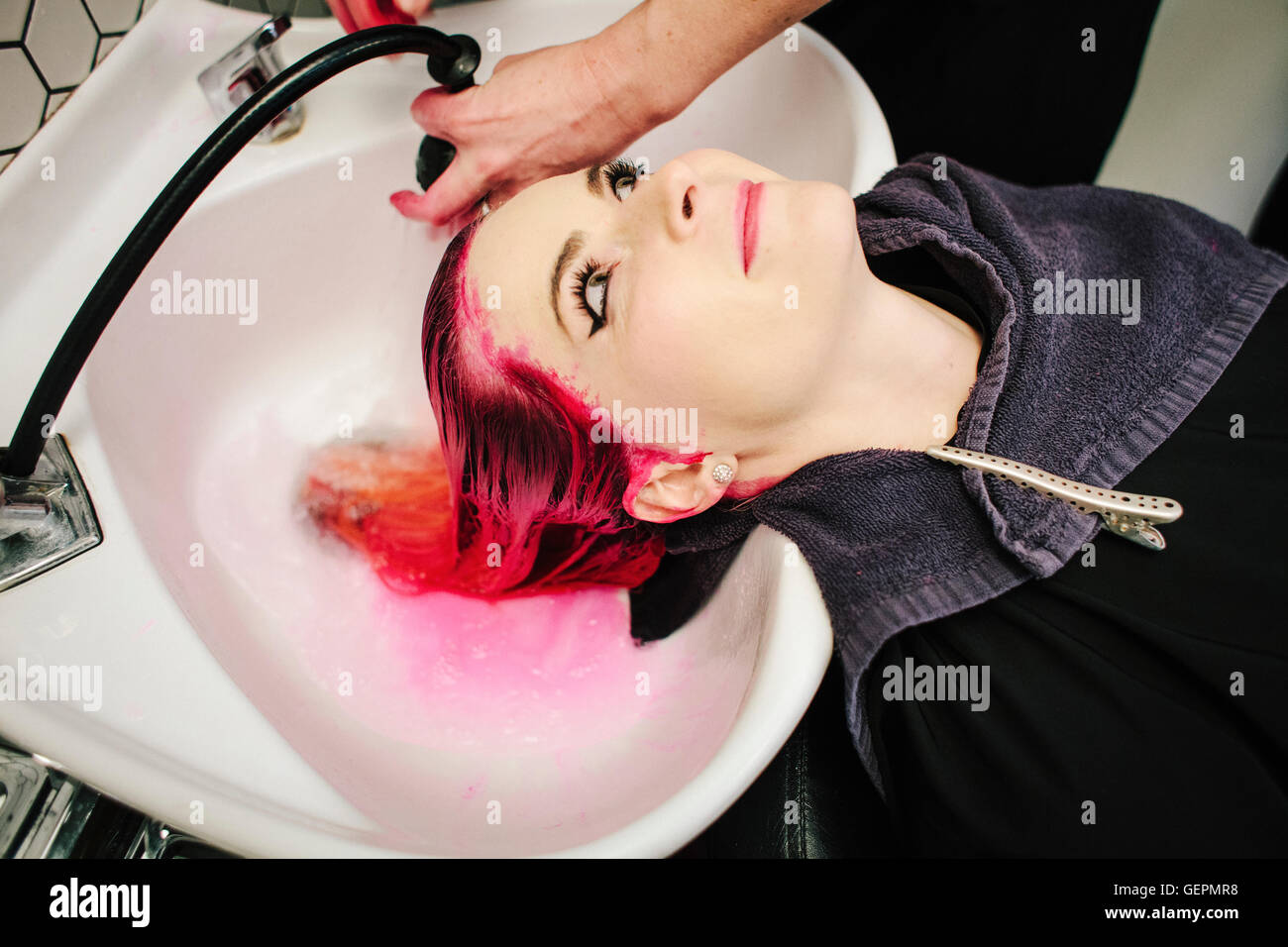 A woman having her hair rinsed with red dye running into the basin ...