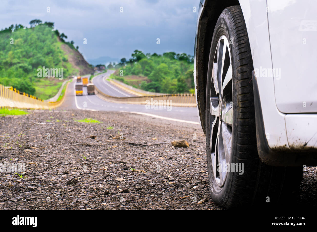 Car wheel against hilly road with trees Stock Photo - Alamy