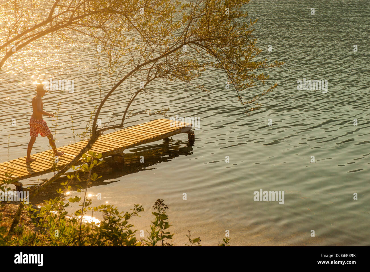 A young boy walks on a jetty in the early evening sun Stock Photo - Alamy