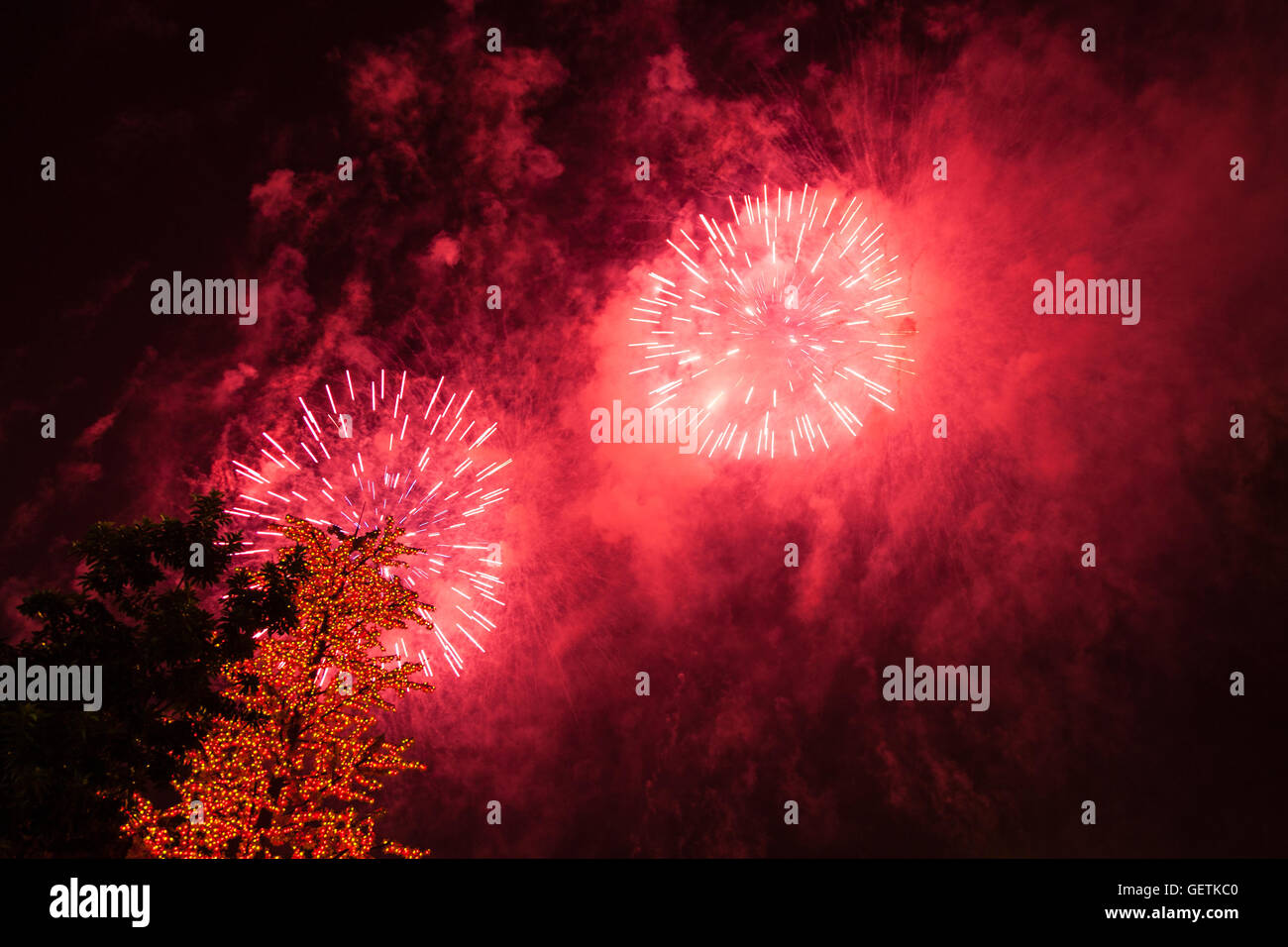 Multiple smoky red fireworks above lit tree Stock Photo - Alamy