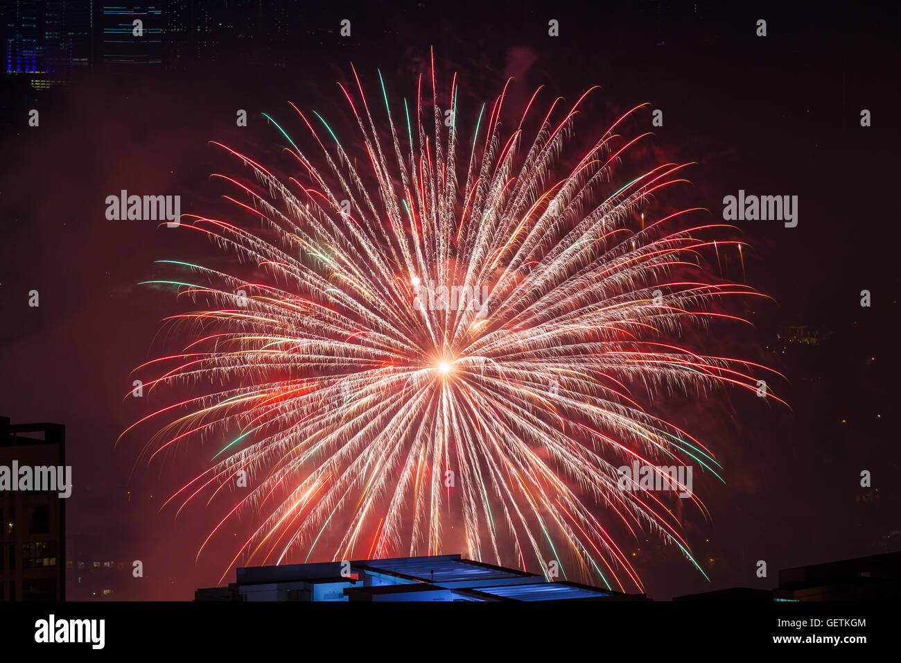 Single red fireworks burst above buildings Stock Photo - Alamy