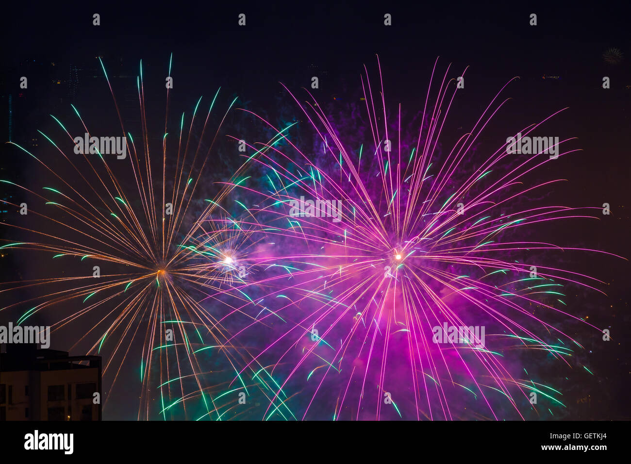 Multi colored magenta fireworks burst above buildings Stock Photo - Alamy