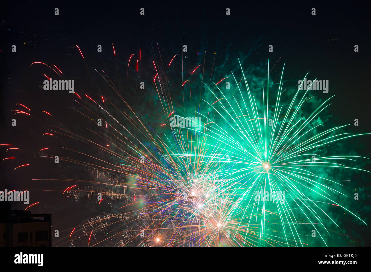 Multiple green orange fireworks burst above buildings Stock Photo - Alamy