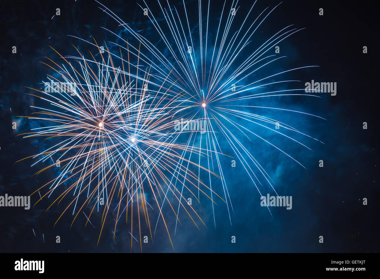 Multiple blue orange fireworks burst above buildings Stock Photo - Alamy