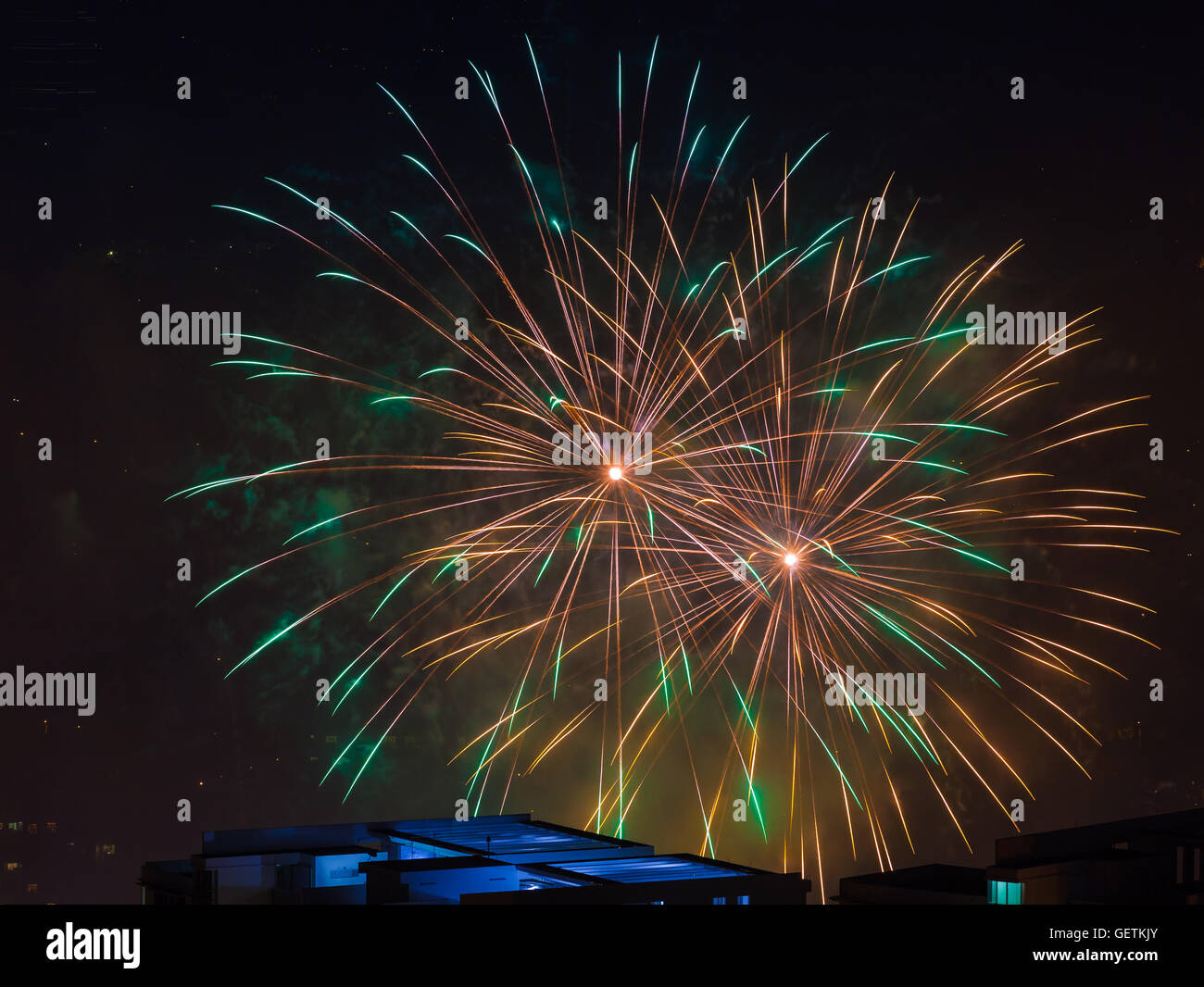 Multiple green orange fireworks burst above buildings Stock Photo - Alamy