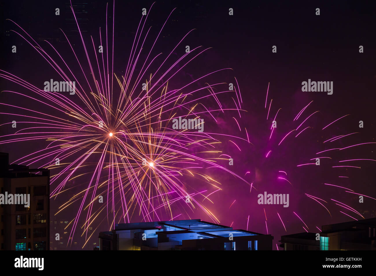 Multiple magenta pink fireworks burst above buildings Stock Photo - Alamy