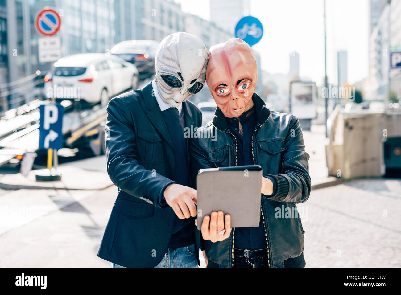 Two man wearing alien masks using tablet hand hold outdoor in city back ...