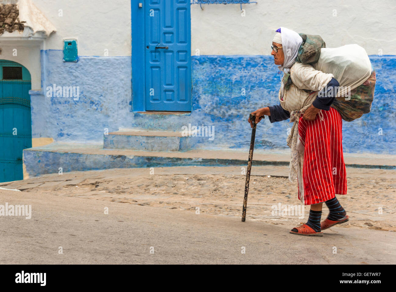 Old woman walking through the streets of Chefchaouen in traditional ...