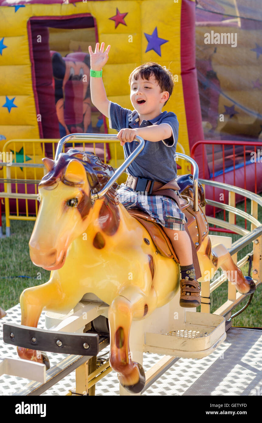 A young boy ride on a ride at a fairground where they sit on toy horses ...