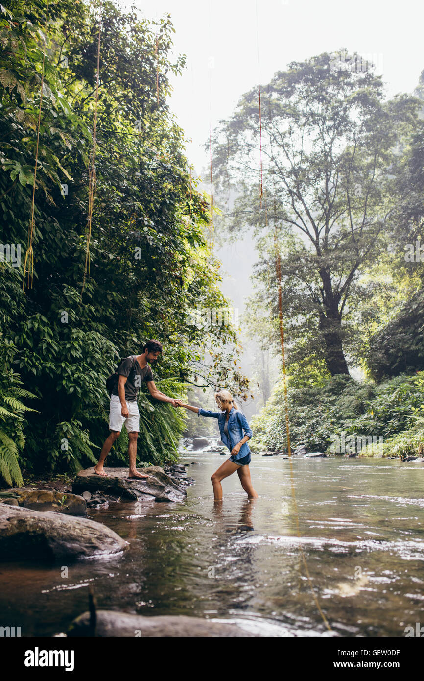 Outdoor shot of young man helping woman crossing stream. Couple in ...