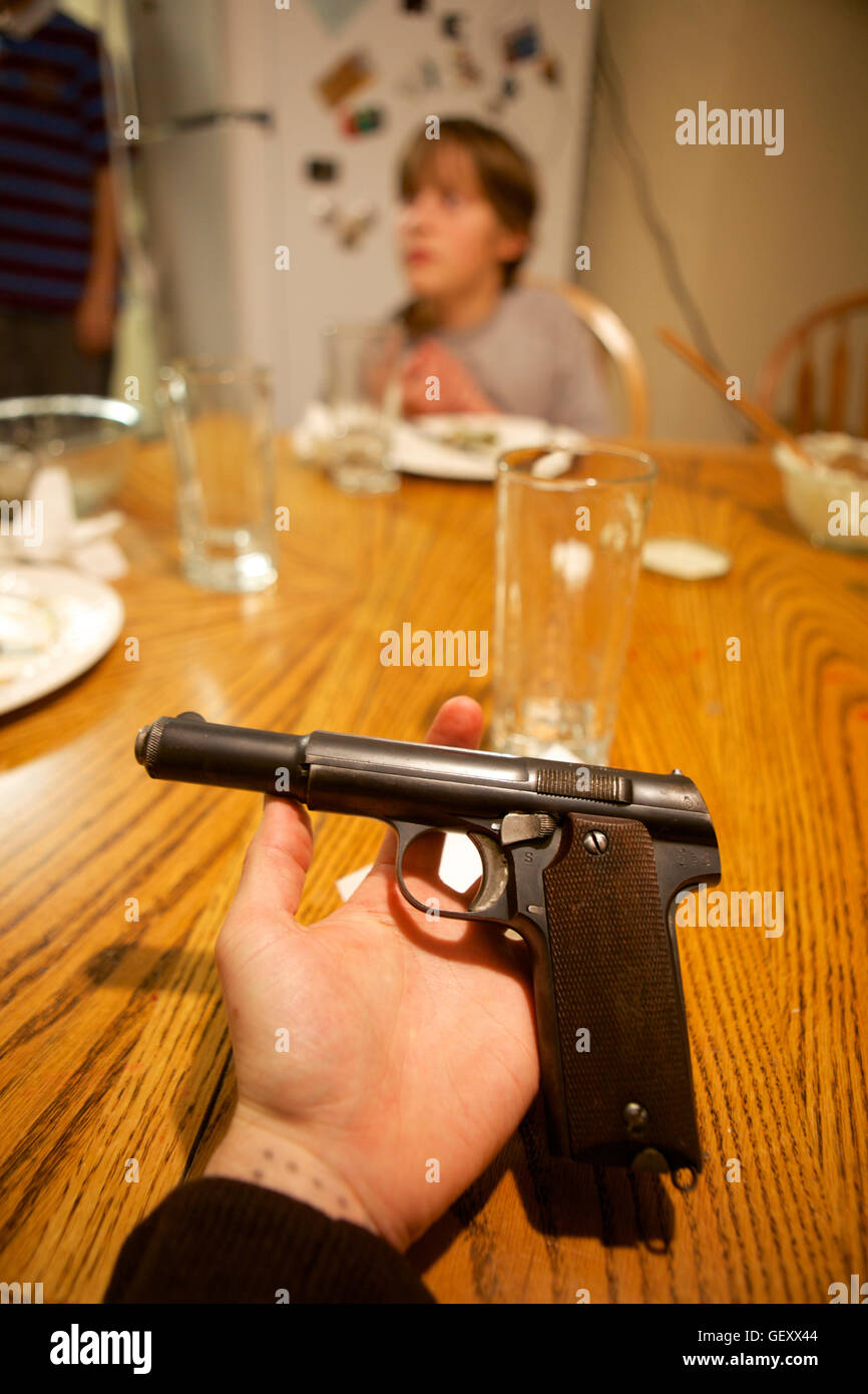 Man holding a pistol at the dinner table with an out of focus child in ...