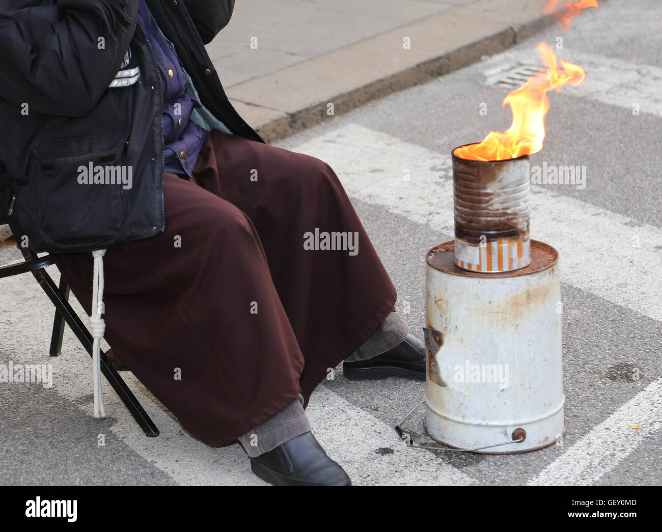 poor friar with brown frock warms up in front of the bonfire in a bin ...