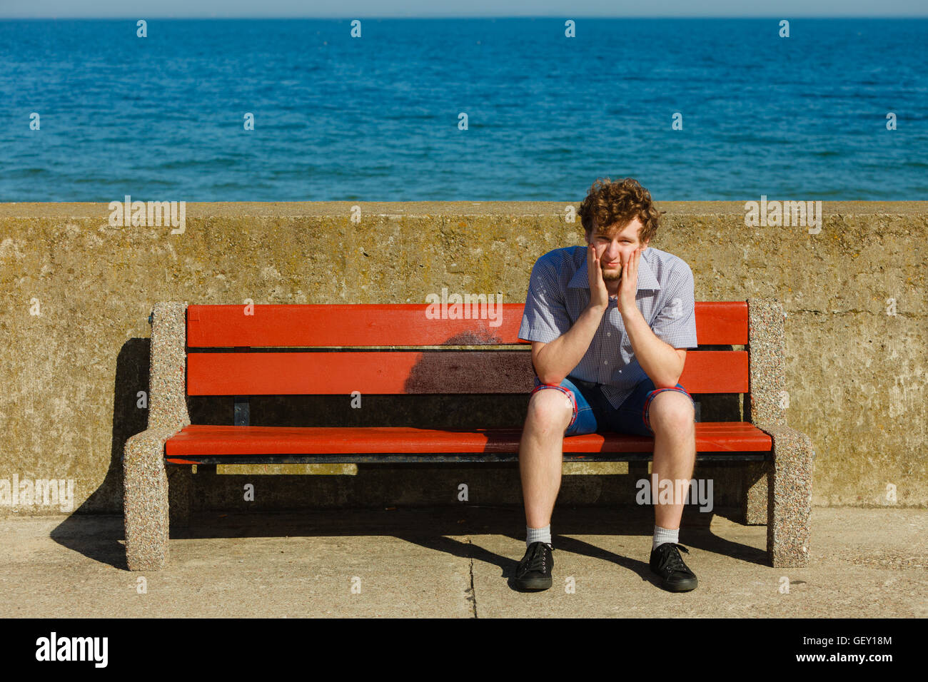Tired exhausted man sitting on bench by sea ocean. Young guy relaxing ...