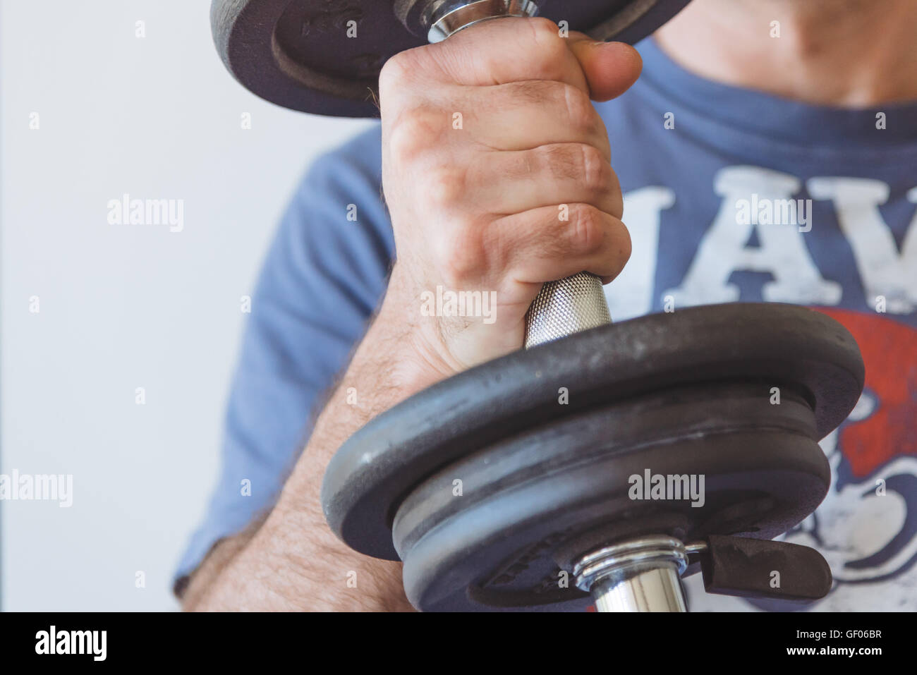 Man doing exercises with dumbbell against a white wall. Focus on hand ...
