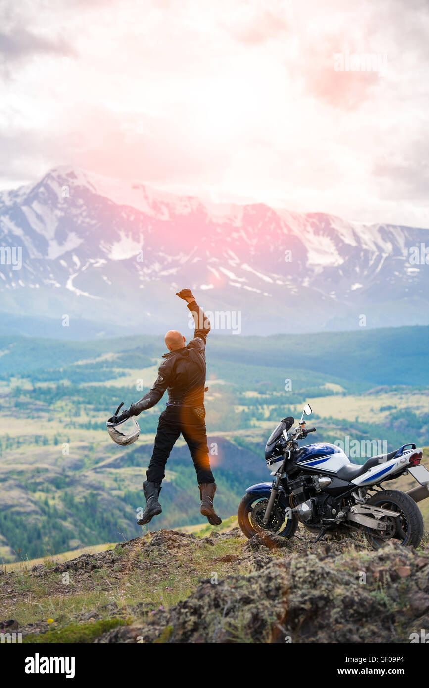Bald rider jumping with hand raised near motorcycle on backgroun Stock ...