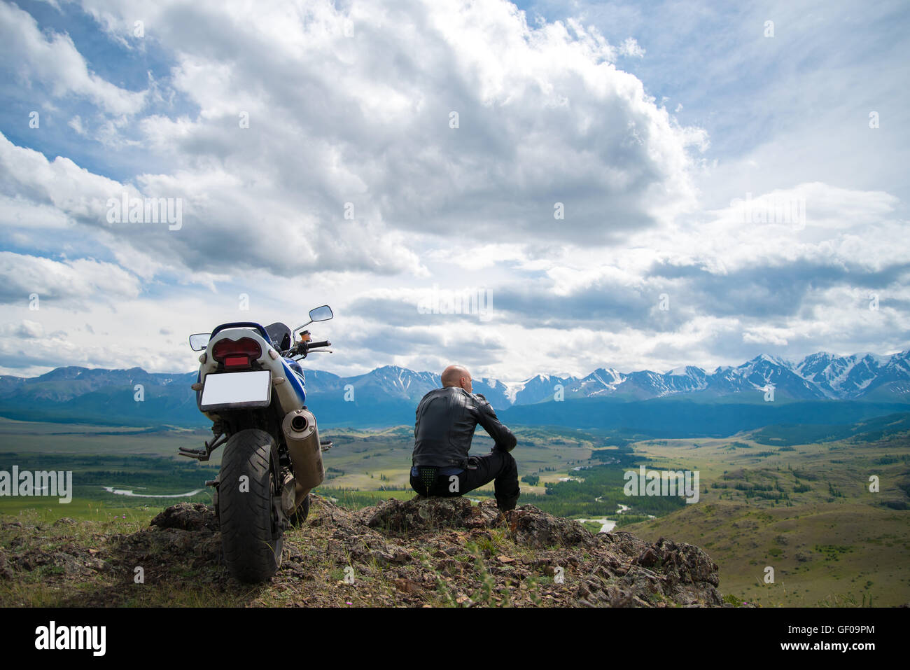 Bald rider sits on a mountain next to motorcycle and looks asi Stock ...