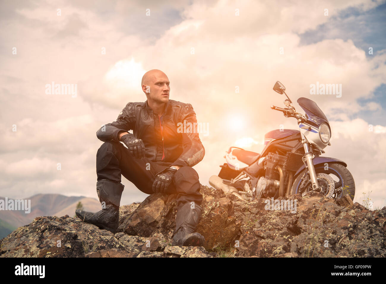 Bald rider sits on a mountain next to motorcycle and looks asi Stock ...