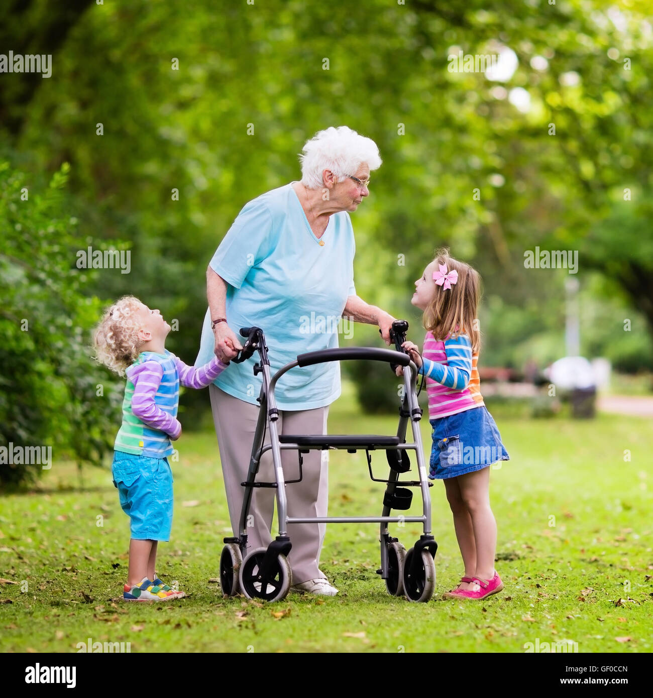Happy senior lady playing with little boy and girl in blooming rose ...