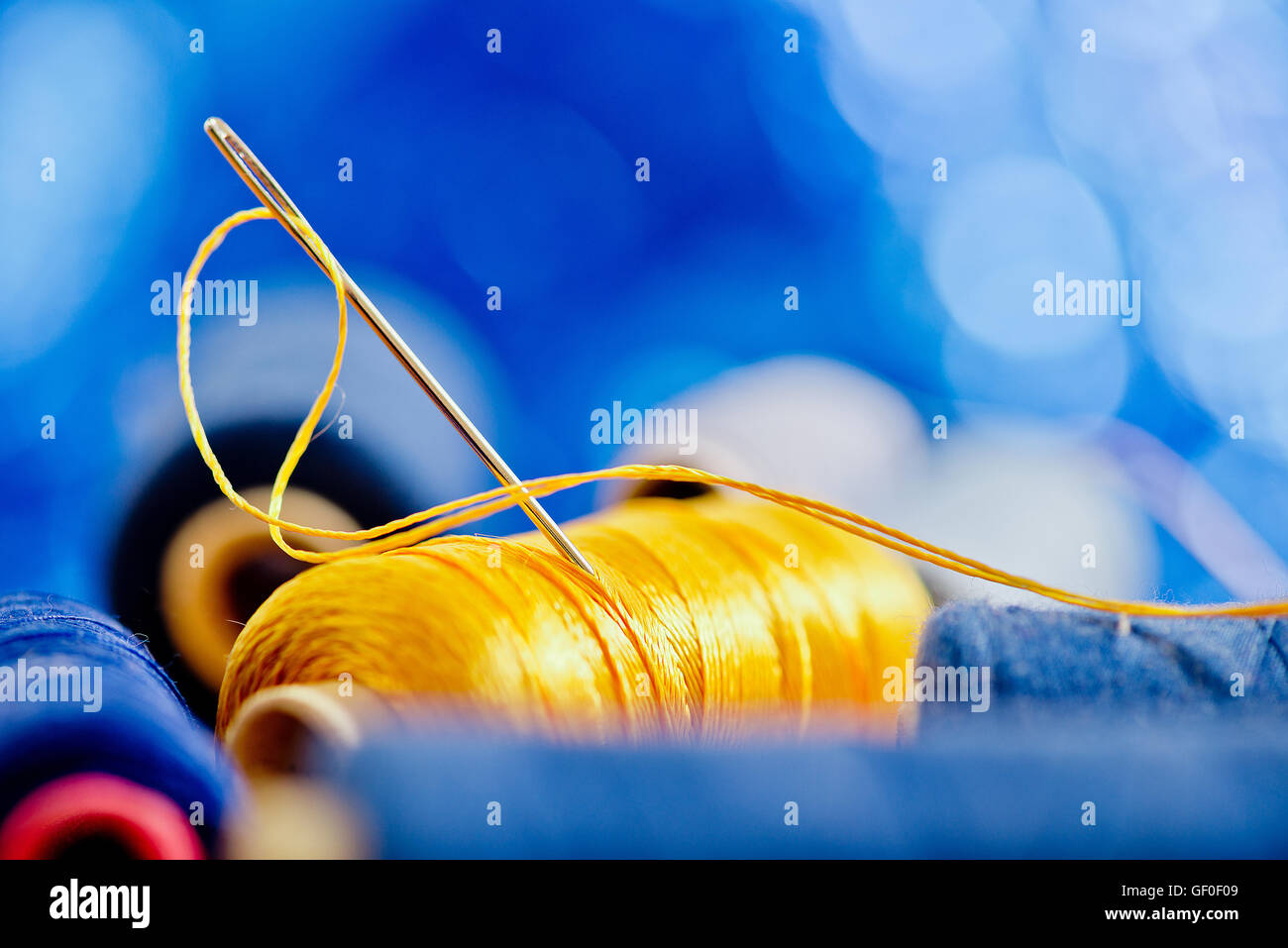 needle and yellow thread on the blue background Stock Photo - Alamy