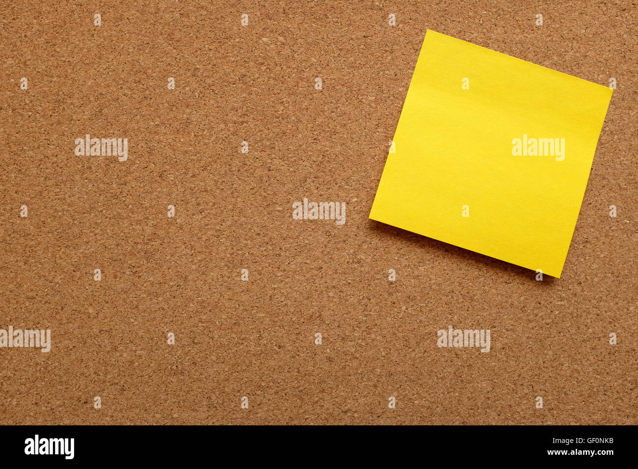 Yellow sticky note stuck on corner of cork pin board with copy space ...