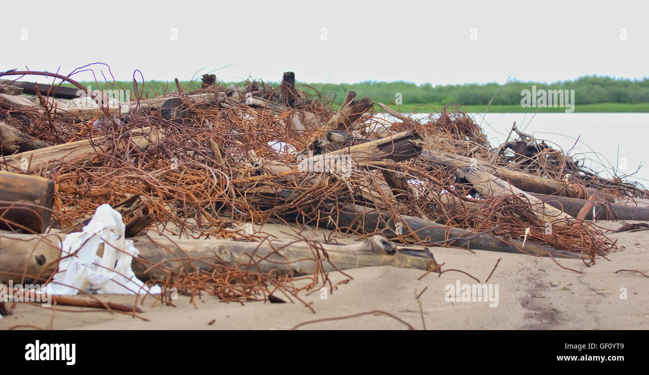 Used steel wire and tree trunks lying at mouth of Siberian river ...