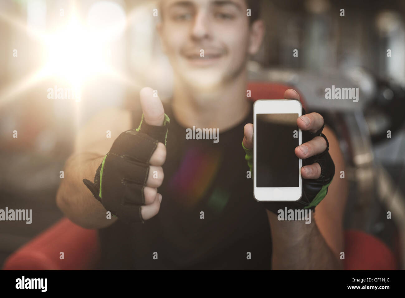 young man with smartphone showing thumbs up in gym Stock Photo - Alamy