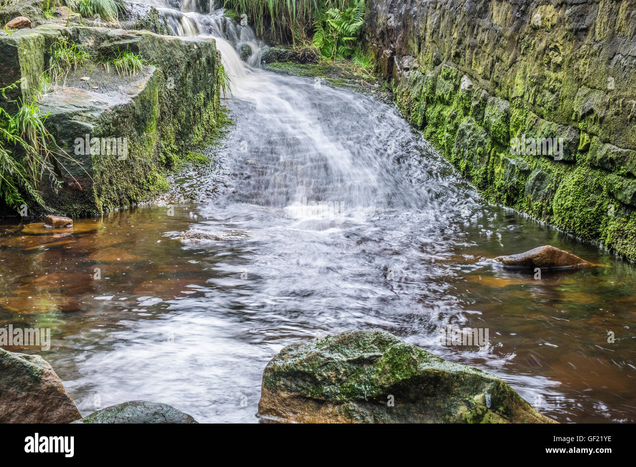 A small stream running over a small waterfall into a larger pool Stock ...