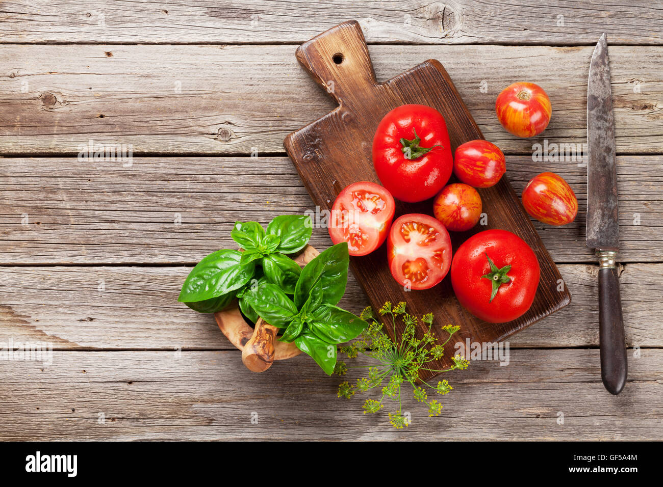 Fresh ripe garden tomatoes and basil on wooden table. Top view with ...