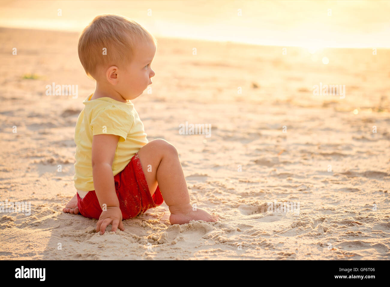 Boy sitting on beach at sunset and looking into sea Stock Photo - Alamy