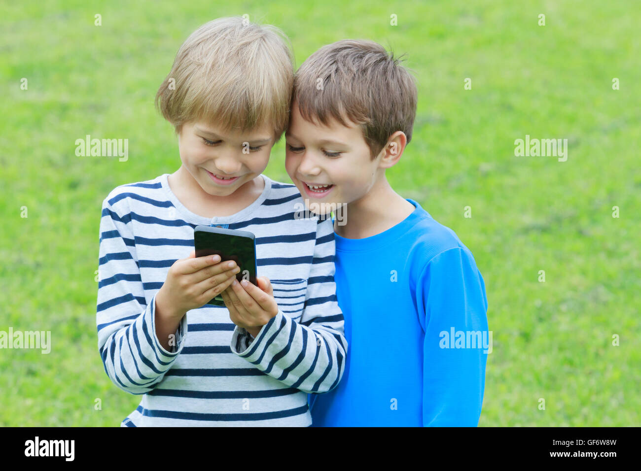 Children with mobile phone outdoor. Two boys smiling, looking to screen ...