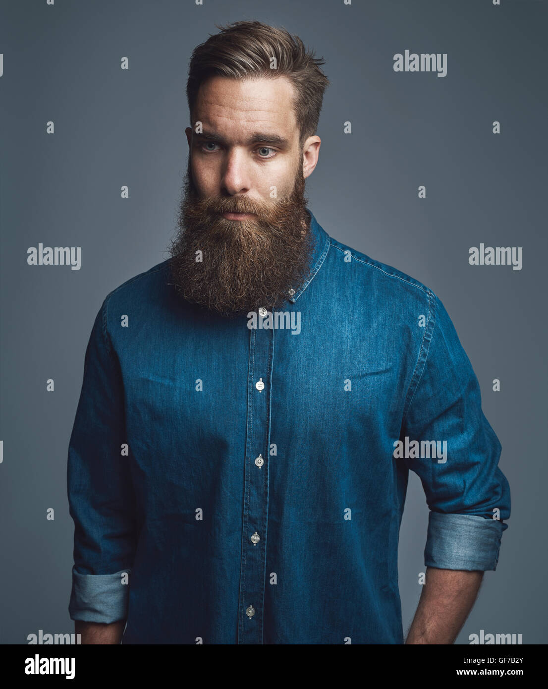 Bearded Man In Blue Denim Shirt With Rolled Up Sleeves And Serious