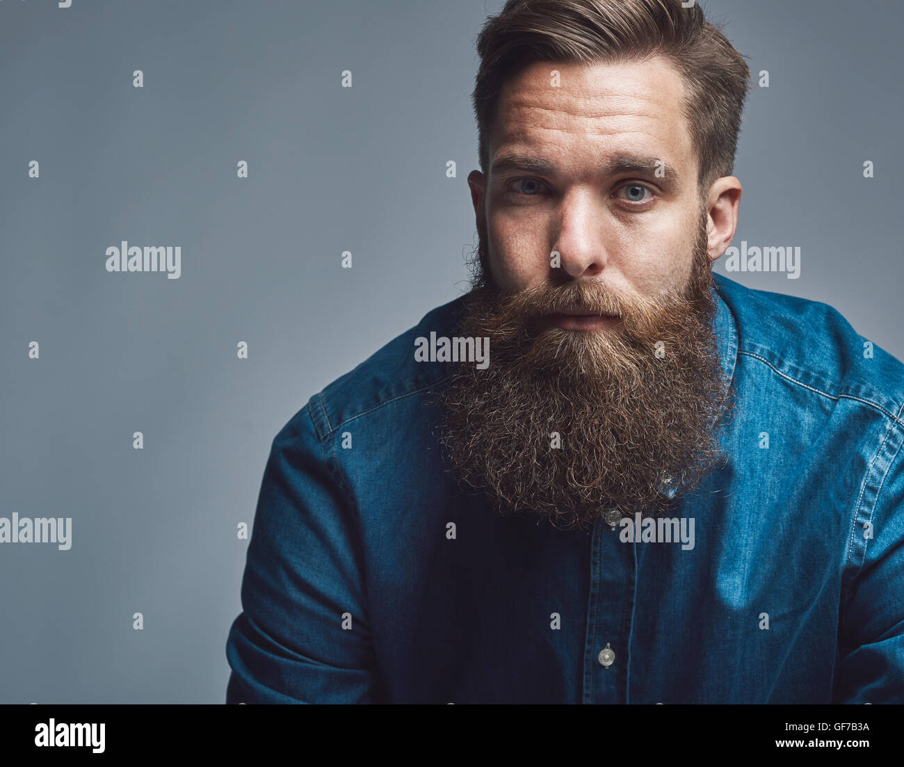Single sitting young handsome serious man in blue denim shirt and beard ...