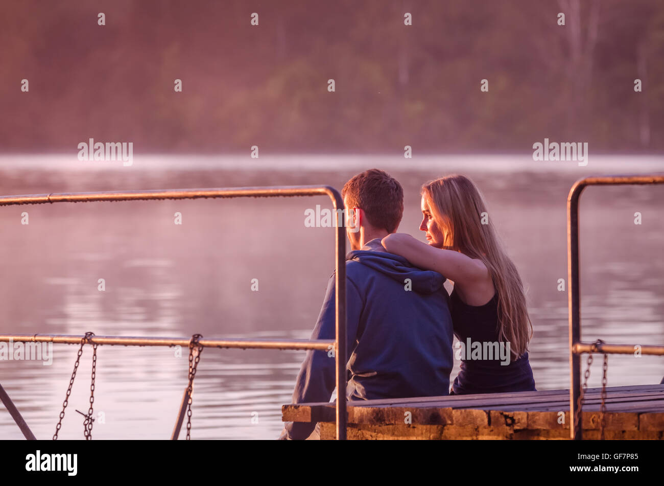 Romantic couple sitting on pier enjoying stunning sunset Stock Photo ...