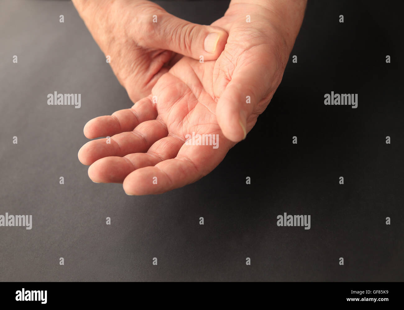 A senior man grips his sore hand on a black background with copy space ...