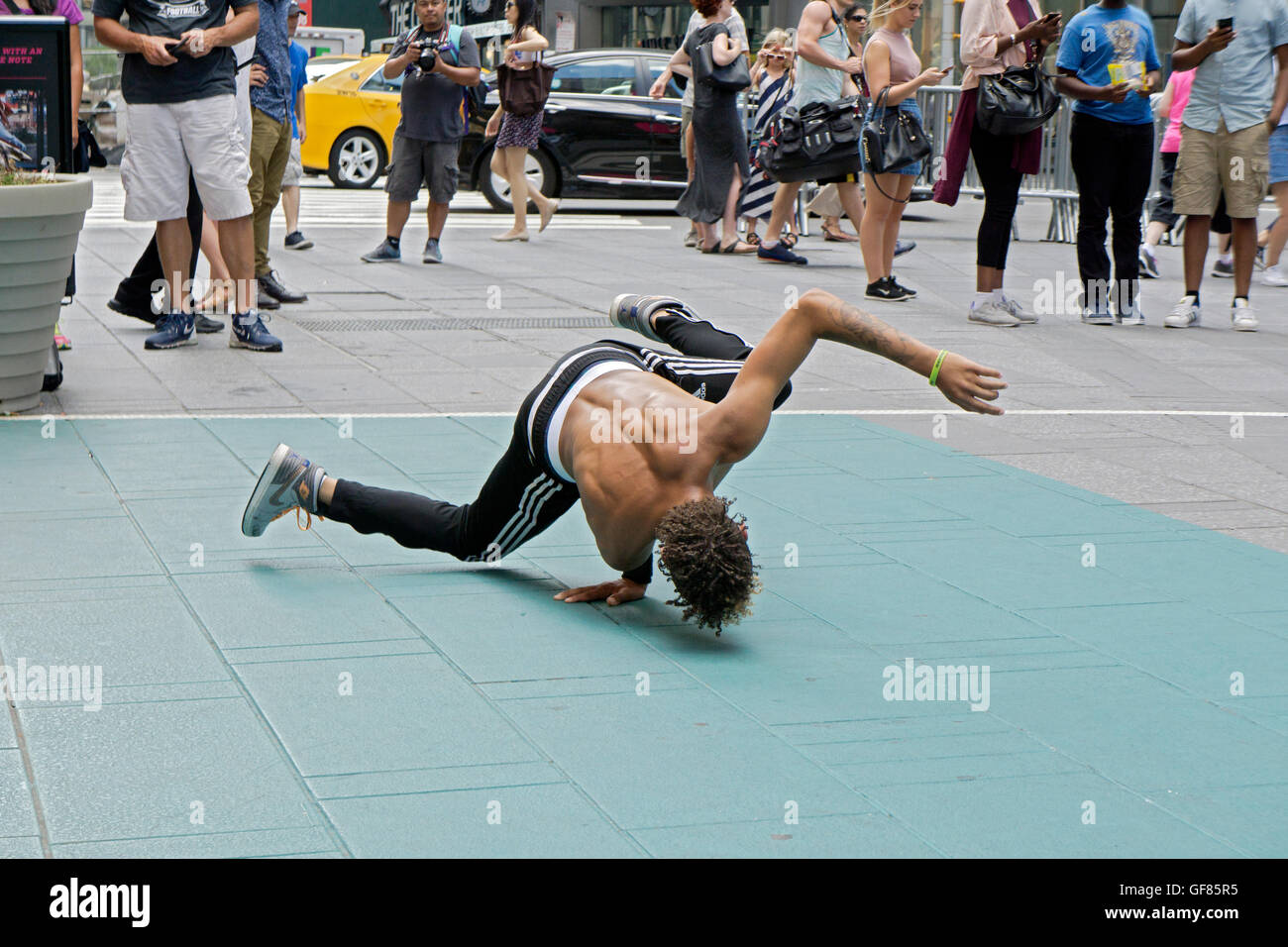 An acrobatic athletic street busker in Times Square does a hand stand ...