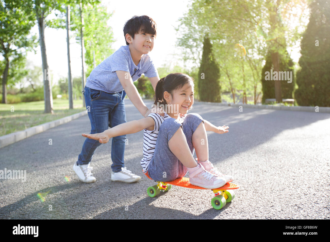 Little Chinese boy pushing girl on skateboard Stock Photo - Alamy
