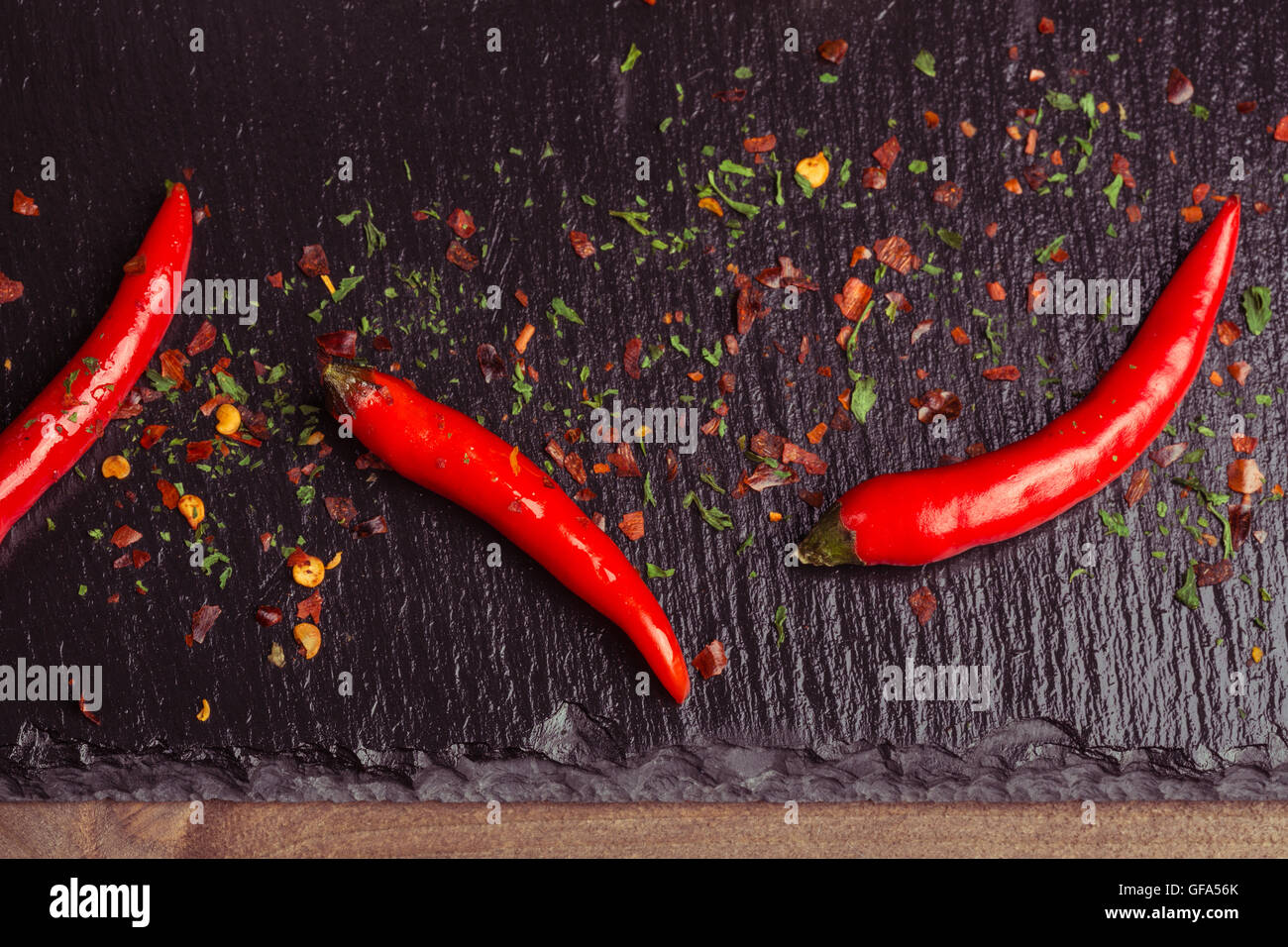 Chillies on a slate with a mixture of chilli flakes and herbs scattered ...