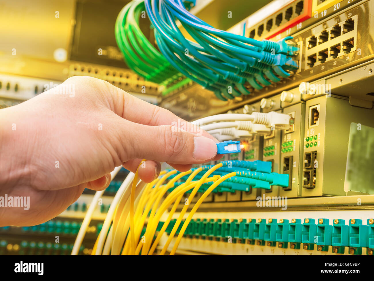 man working in network server room with fiber optic hub for digital ...