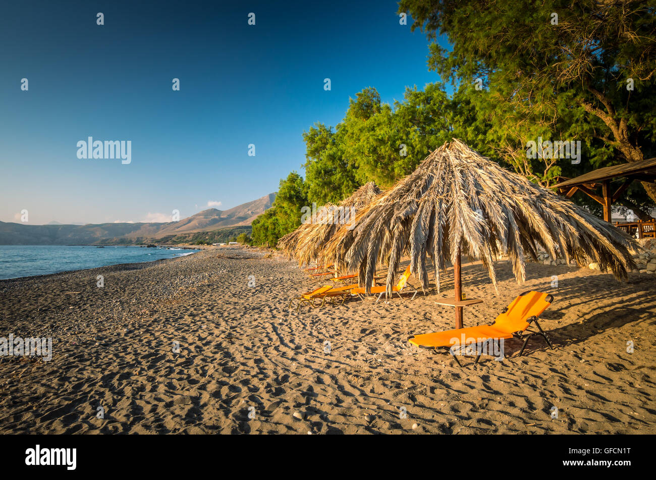 Sfinari Beach in Crete island, Greece. Straw parasols and sunbeds on ...